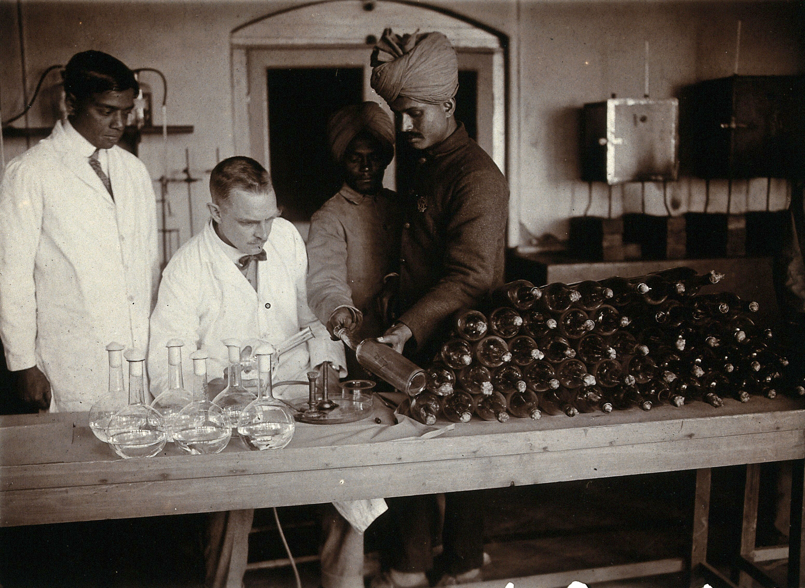 A laboratory with staff (Indian and British ?) at work at a table piled ...