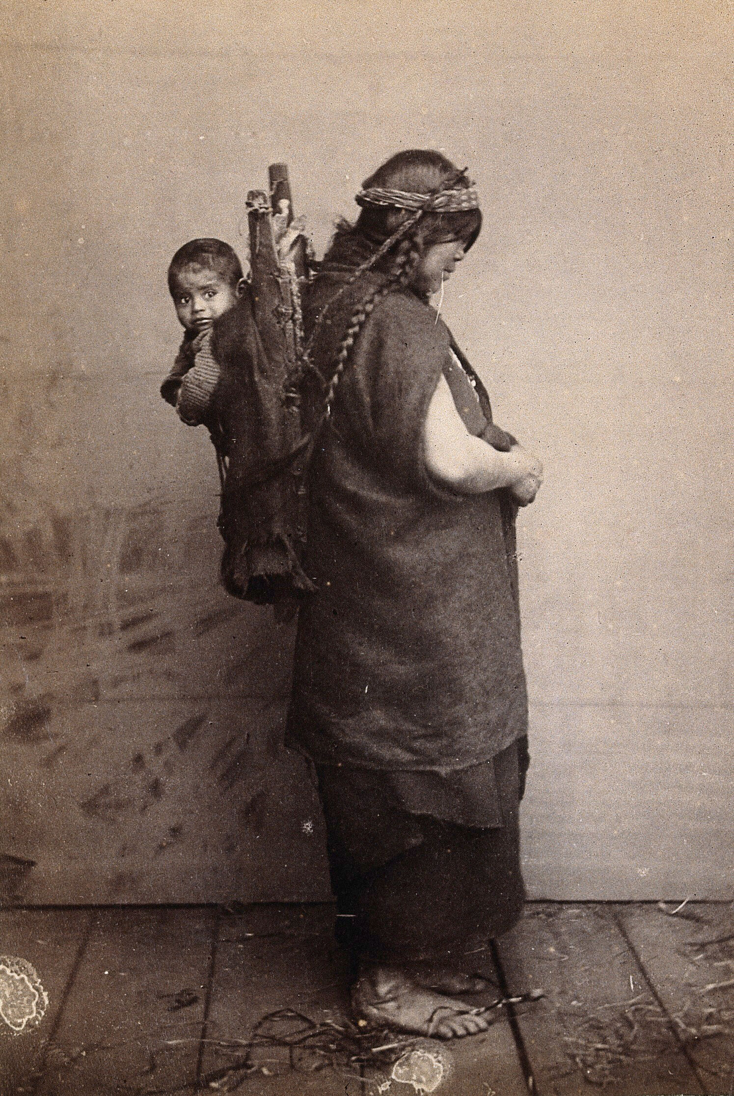 A woman (Native American?) carrying a child on her back in a wooden ...